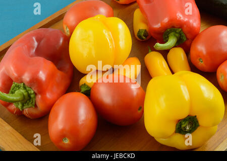 Red bell peppers in a wooden box and tomatoes on a dark background ...