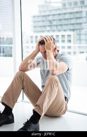 Tensed man sitting against window Stock Photo - Alamy