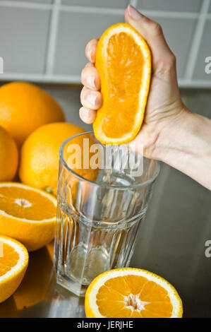 One hand squeezing one half orange, orange slices and orange juice on a ...
