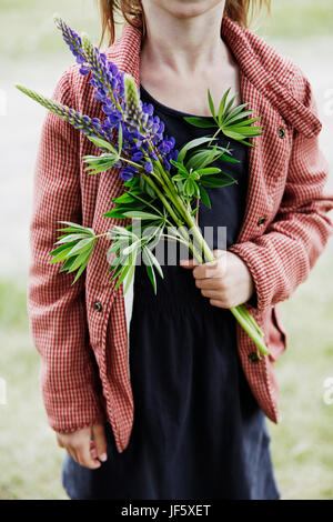A blonde girl in a flower lupine wreath with a bouquet of lupines ...