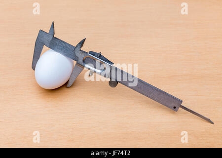 Vernier caliper measuring white chicken egg on wood Stock Photo - Alamy