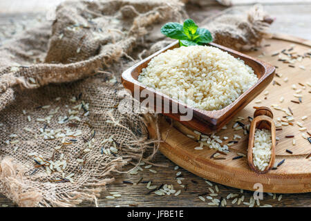 Raw round white rice in a wooden bowl and in a wooden spoon on a wood ...