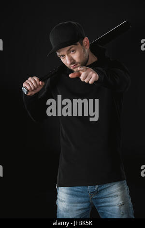 young robber in zoodie and cap with baseball bat isolated on black ...