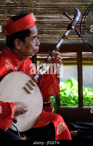 Vietnamese man playing a moon lute (Đàn nguyệt), a two-string plucked ...