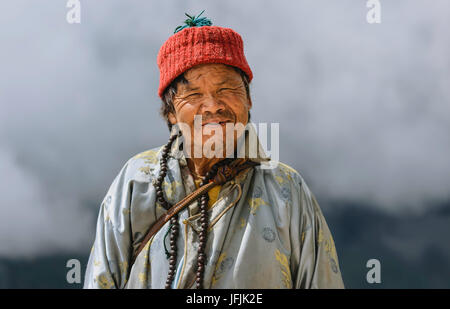 Portrait of man from the Monpa tribe sitting outside his wooden house ...