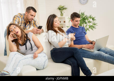 Four bored friends hanging out in an apartment and using smart phones ...