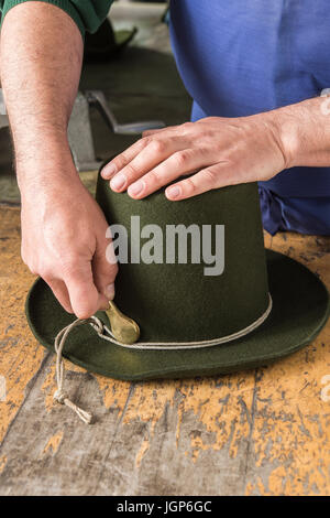 Tightening the shaping cord around a wool felt hat, using iron tool ...