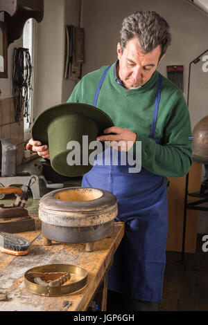 Hatter holding dry wool felt hat in an edge mold, hatmaker workshop ...