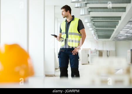 Workers wearing hi vis vest, standing in newly constructed office space ...