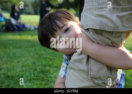 Boy clinging to his father's leg, looking at camera, cropped view Stock ...