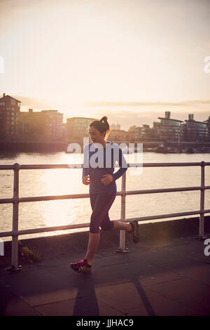 A woman running alongside the River Thames with Tower Bridge in the ...