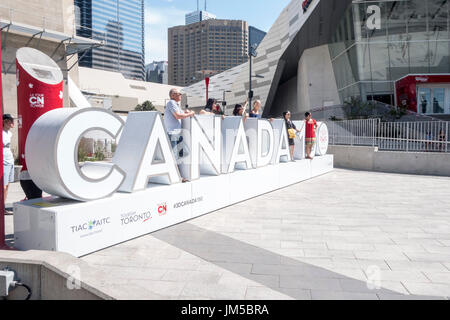 Tourists posing at the Canada 150 sign outside of the CN tower in ...
