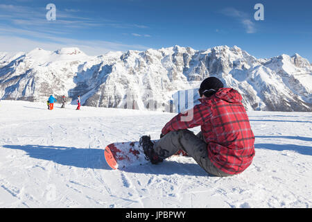 Tired snowboarder sitting on snow covered landscape while looking at ...