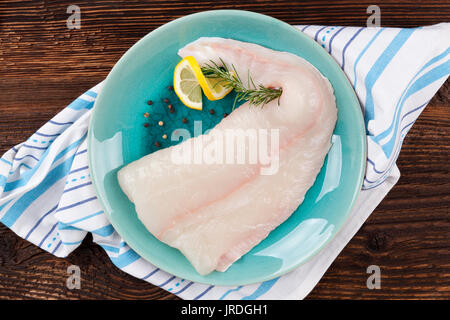 Fresh halibut fillet with lemon and rosemary on plate on wooden table ...