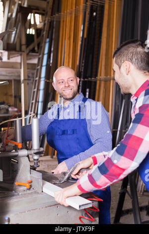 Two happy workmen in uniform working on a machine in PVC shop Stock ...
