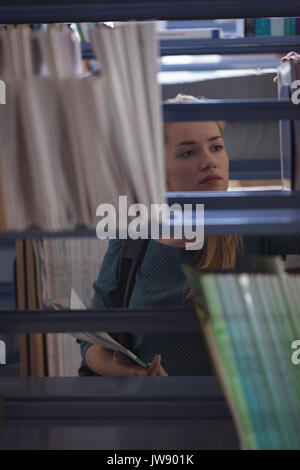 In the library - pretty female student with laptop and books working in ...