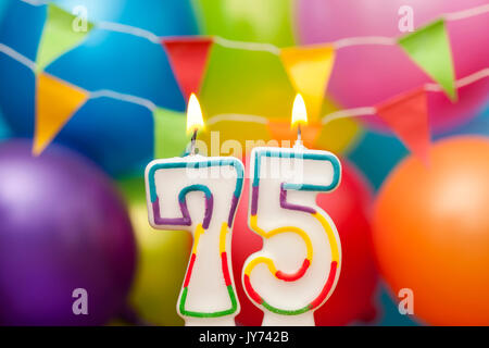 Number 75 candle with party balloons on a bright yellow background ...