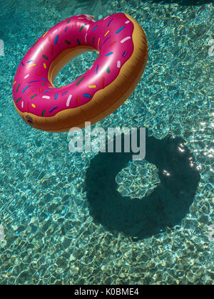 Pink donut-shaped inflatable float in turquoise swimming pool with ...