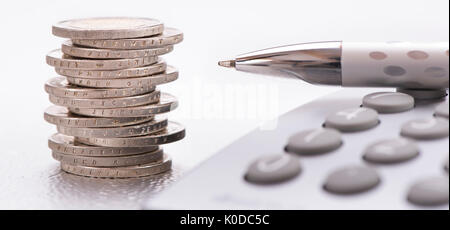 A stack of paper money and coins and a calculator on a light gray ...