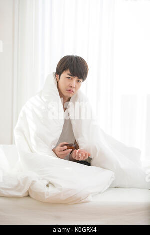 Asian man wrapped in blanket feeling unwell at home with medicine Stock ...