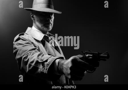 Undercover spy agent pointing a gun in the dark, 1950s noir film male ...