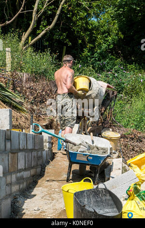 Labourer on building site mixing cement and adding water using a mixer ...