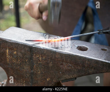 Blacksmith hammering hot iron rod on anvil against the background of ...