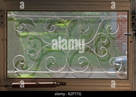 Mid-century decorative screen grate on a window in a door with grass ...