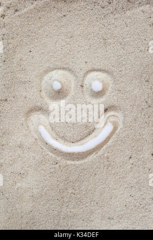 Face drawn in the sand on the beach, with sunglasses. Sand with wave ...