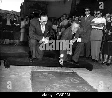 Van Johnson putting a date to his hand and footprints in wet concrete ...