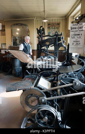 older male printer working vintage flatbed printing press surrounded by ...