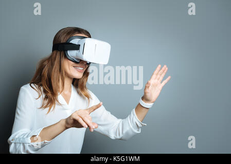 Virtual technology. Happy delighted nice girl smiling and looking at ...