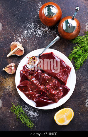 Pieces of raw liver on a wooden cutting board against a dark concrete ...