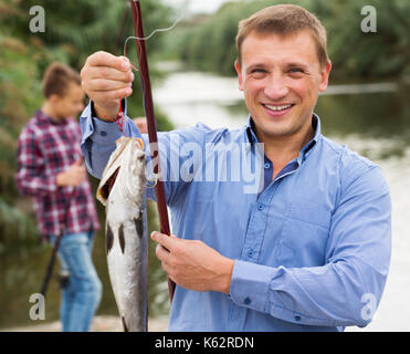 Glad man holding a fish after fishing on a river side Stock Photo - Alamy