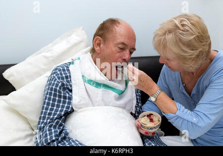 An elderly sick bedridden man being fed breakfast by his wife and carer ...