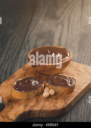 Wooden board with bowl of hazelnut butter on color background, closeup ...