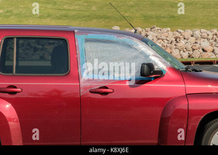 A red automobile with a broken passenger window, taped up with plastic ...