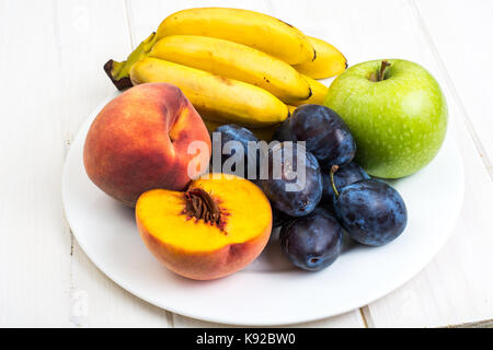 Assorted ripe fresh plums, bananas, peaches and apples on white table ...