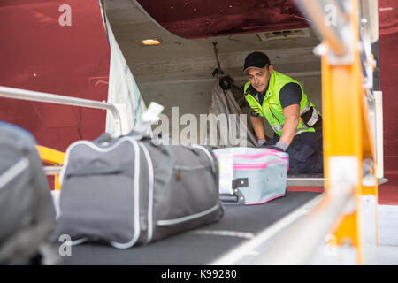 Aircraft ramp loader loading baggage to conveyor belt on airport apron ...