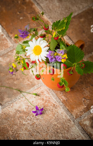 Ripe strawberries and a bouquet of forest flowers in a clay mug Stock ...