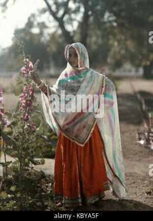 A girl of Agra stands next to a flower bush in traditional clothing by ...