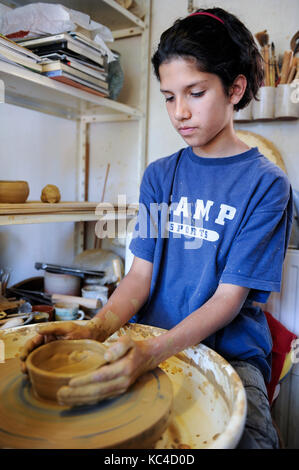 Germany, boy learning pottery, making pots from clay at turning wheel ...