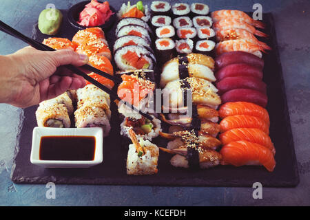Japanese sushi big set with hand holding one in wooden black chopsticks ...
