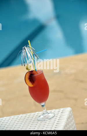 a colourful cocktail with straws and umbrella next to a swimming pool ...