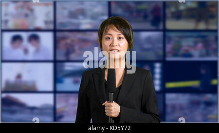 Asian American female news anchor in studio with screens in background ...