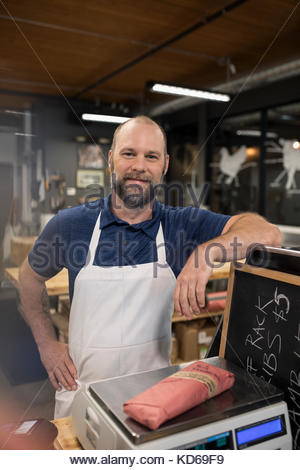 Smiling male butcher weighing on scales piece of meat in butcher’s ...