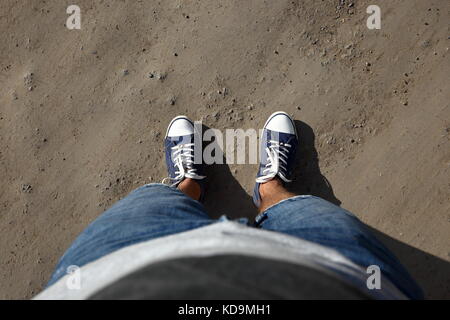 Looking down pov point of view on legs feet in jeans with sports shoes ...