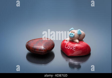 Figurine of a cute little pig lying on a red heart-shaped stone with ...