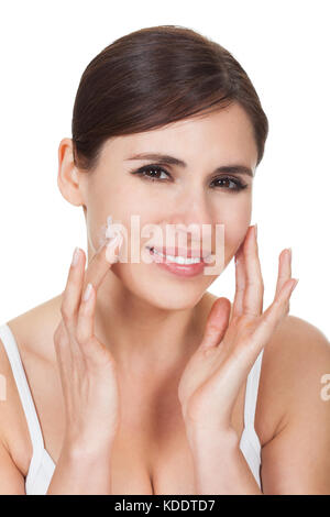 Attractive young woman applying moisturizer on her face while standing ...