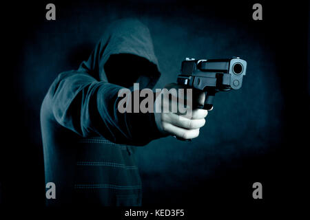Hooded man with a gun in the dark Stock Photo - Alamy
